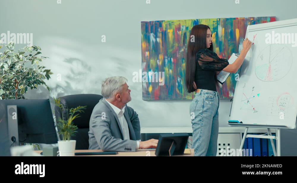 Young assistant to the boss stands next to chart board, explains ...