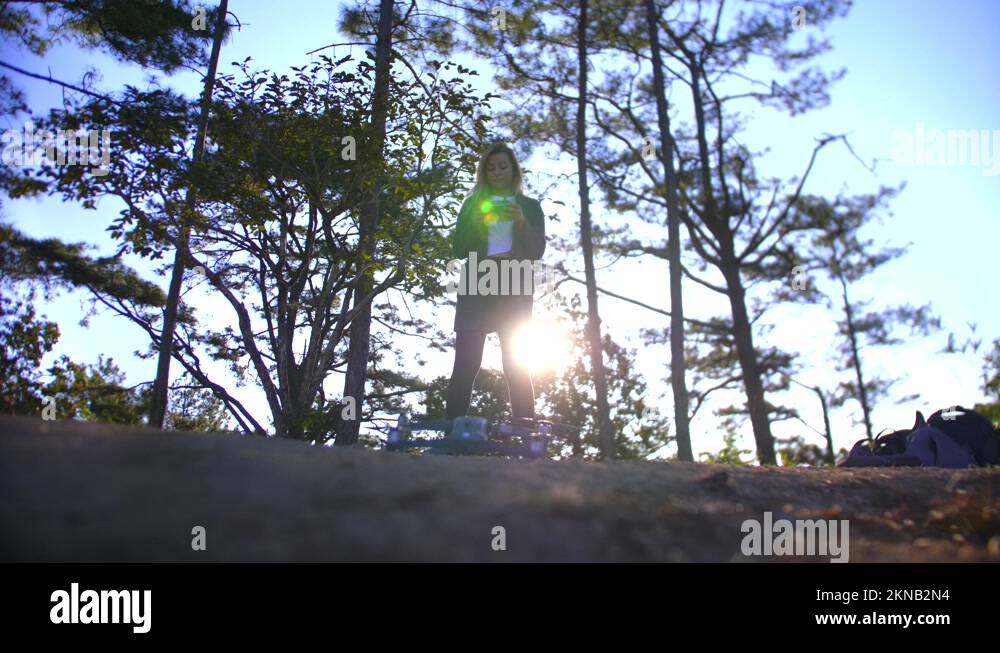 Blonde girl starting a drone on a dusty ground, on a sunny evening, in ...