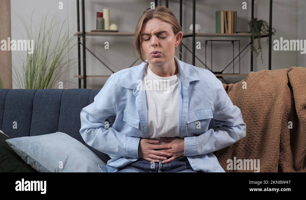 Sick blonde woman suffering from stomach ache sitting on sofa Gastritis ...