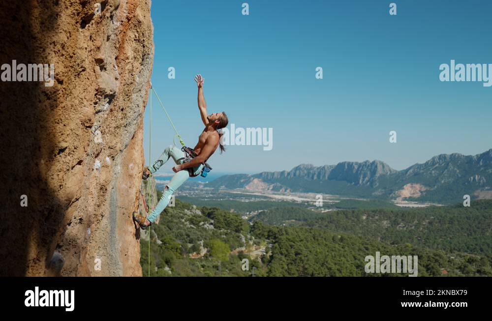 handsome strong and fit man rock climber with long hair hangs on rope ...