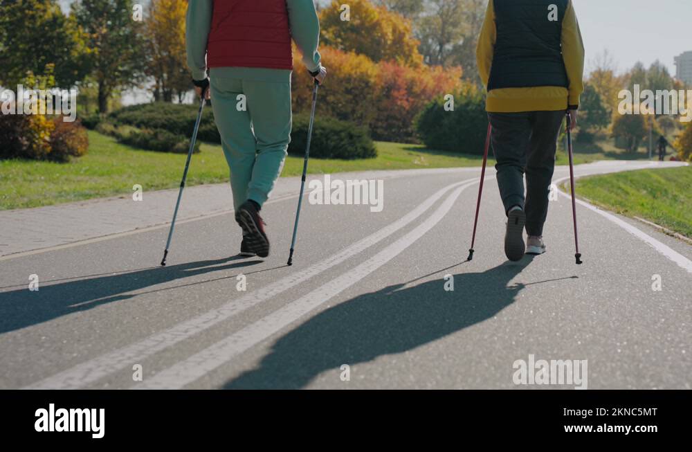 Shot of legs of two people doing Scandinavian walking in fall park ...