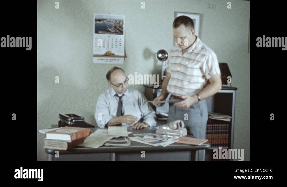 1950s: Reverse action: Two men sit and they look at photos together ...