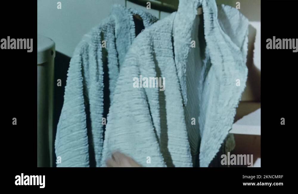 1950s: Salesman and customer look at hanging robes. Woman inspects ...