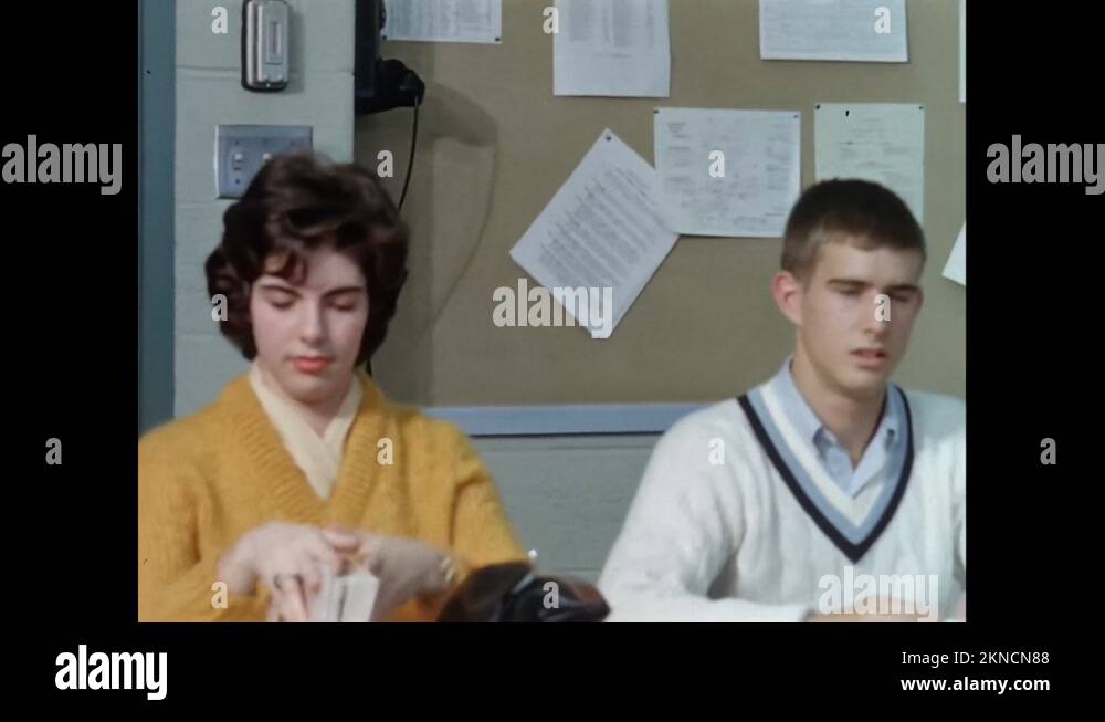 1960s: Students open books at desks in classroom. Teenage girls shake ...
