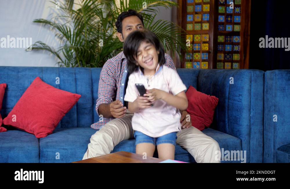 An adorable little kid and his Indian dad watching television together ...