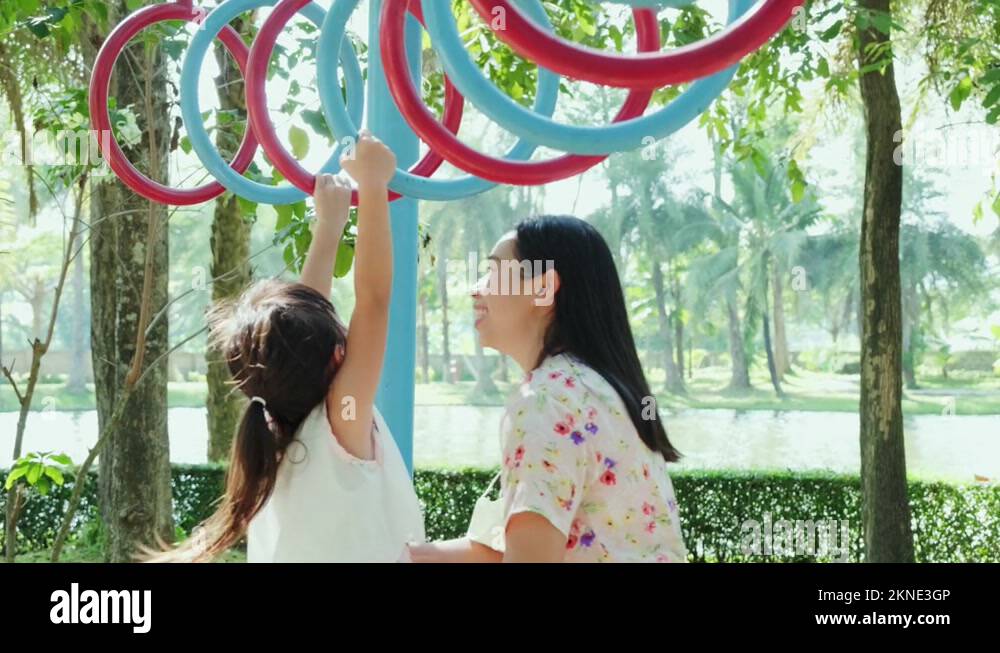 Mother helps her little daughter to hang on colorful monkey bars in ...