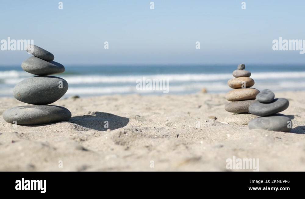 Rock balancing on ocean beach, stones stacking by sea water waves ...
