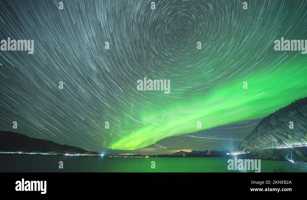 Starry sky and northern lights above the fjord. City lights in a ...