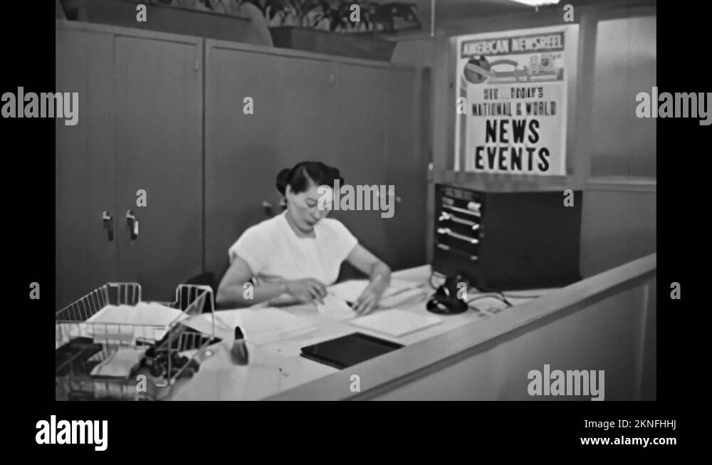 1950s: Man operating film camera. Woman sitting down at office desk ...