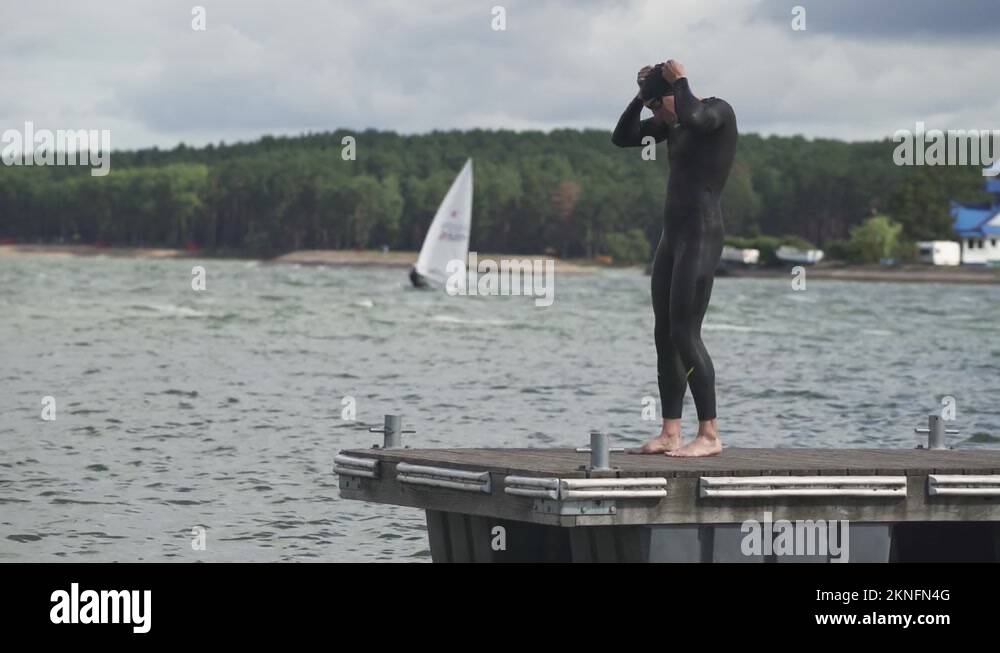 Pro swimmer, triathlete in wetsuit for swims walks along the pier and ...
