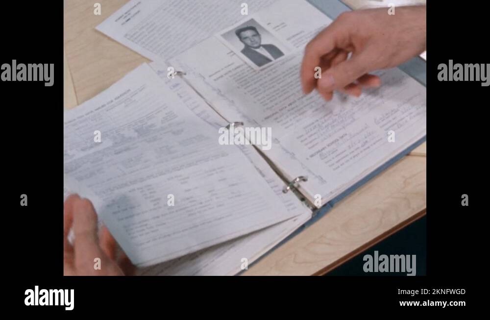 1960s: Hand holding clapperboard. Hands turning pages in three-ring ...