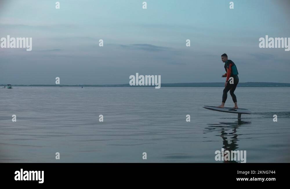 Man riding on a hydrofoil surfboard on large blue lake at the pink ...