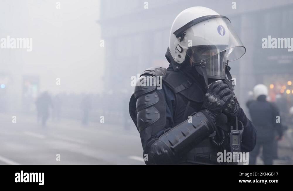 A single police officer in full riot gear places a gas mask on his face ...