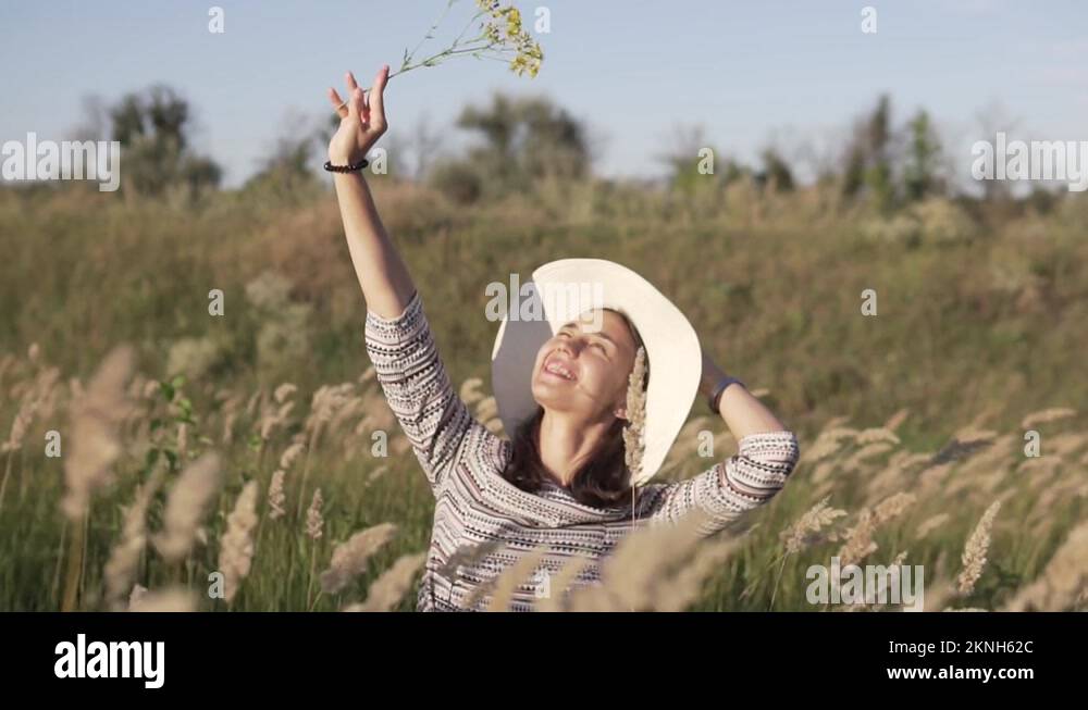A beautiful young girl in a straw hat squints in the sun. She waves her ...