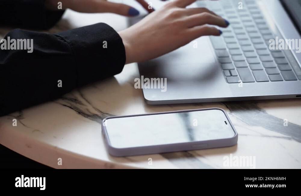 A young woman is typing on a laptop and talking on the phone while ...