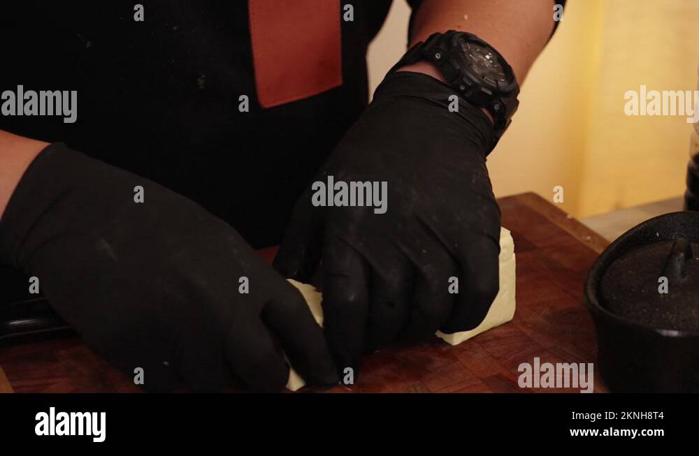 Faceless chef with black gloves breaking down chunk of organic butter ...