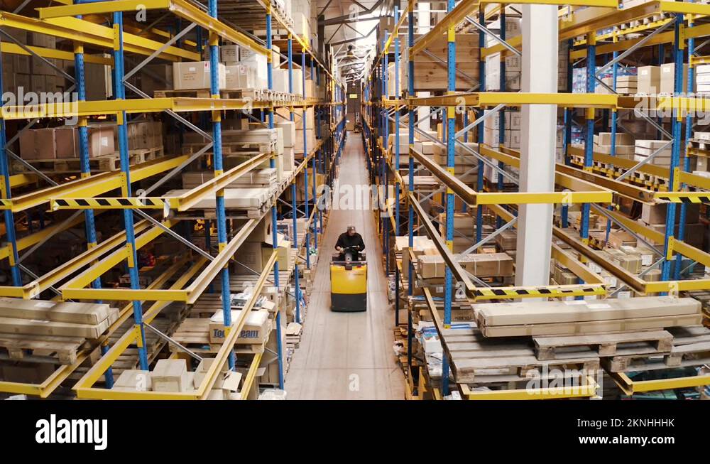 Man driving an electric cart through a storage warehouse aisle,aerial ...