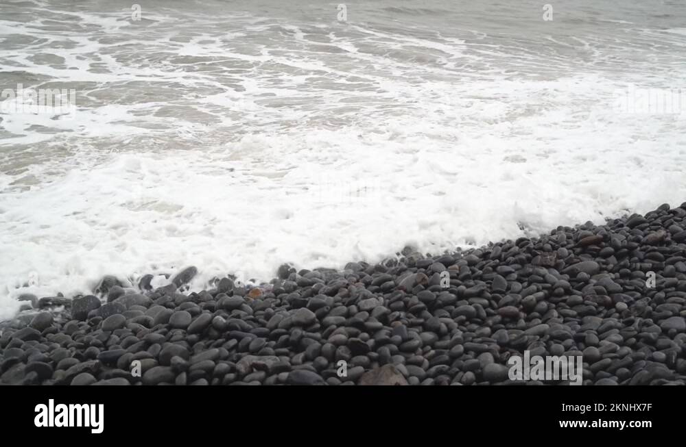 Pan right to left across Winter Tide splashing in over rocky beach at ...