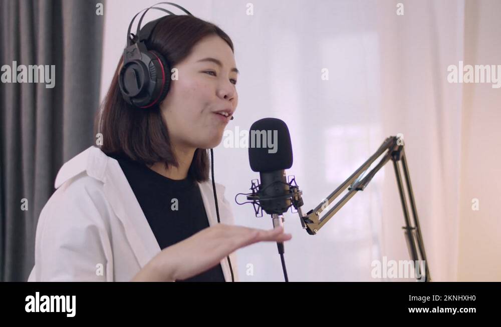 Young Asian female podcaster talking into a microphone while recording ...