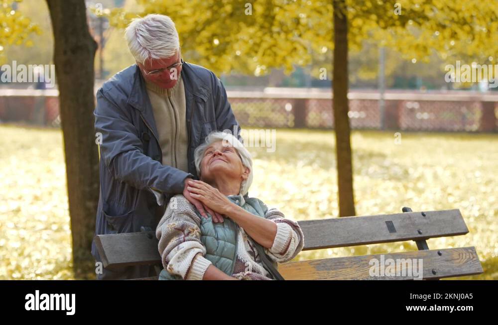 Elderly couple in the park. Man placing his hand over the shoulder of a ...