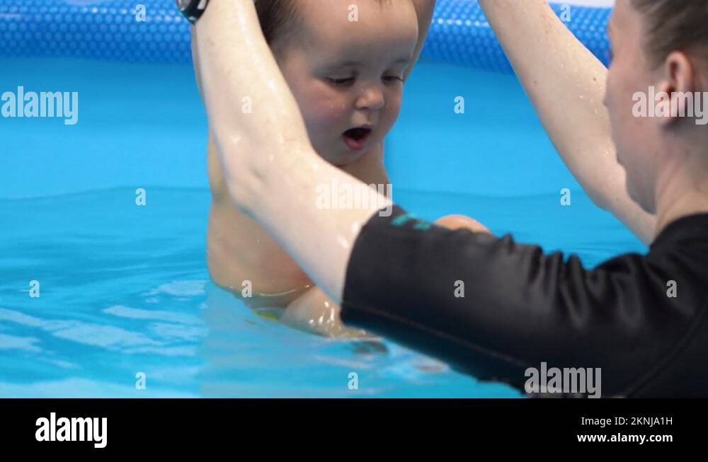 Newborn child train and learn to swim in pool with an instructor. Slow ...