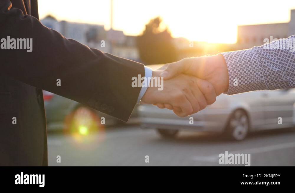 Two businessmen shaking hands of each other with cars in parking at ...