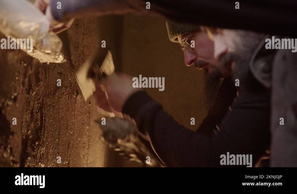 Two friends using clay to render walls in an old house, doing up a ...