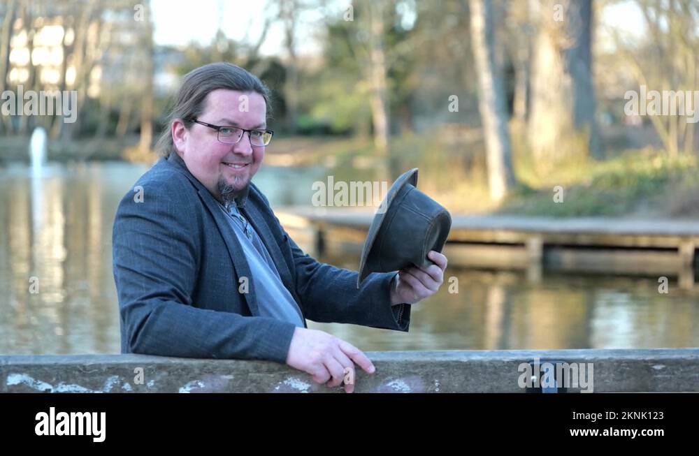 [4k] long haired man sitting on park bench waving with his hat to come ...
