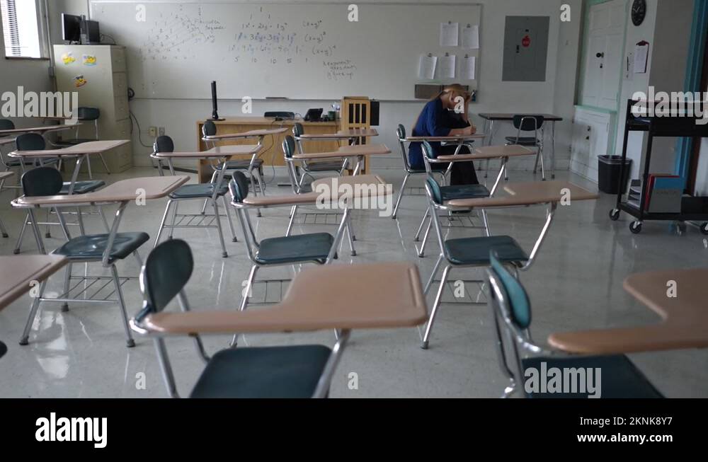 Female student works at her desk alone in a darkened empty school ...