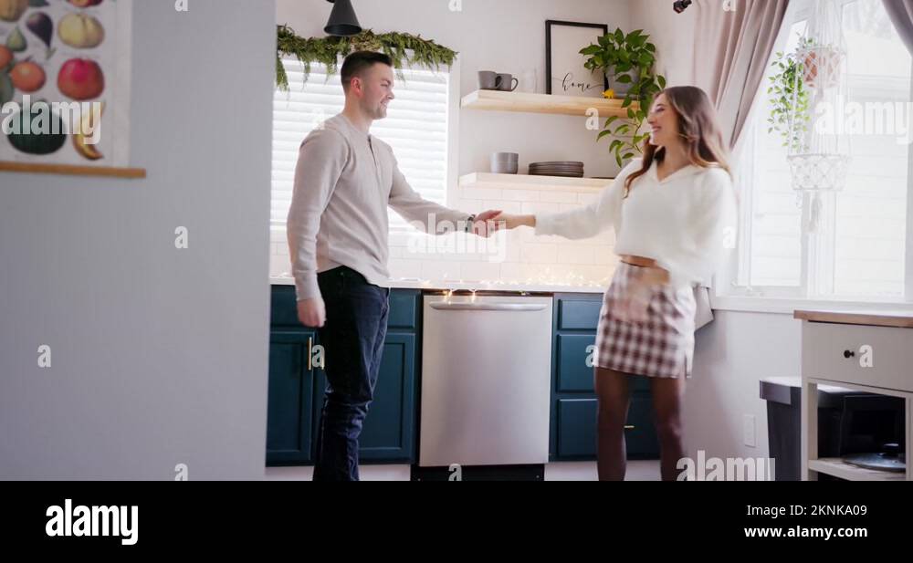 Romantic couple hugs, smiles and kisses in a bright kitchen while ...