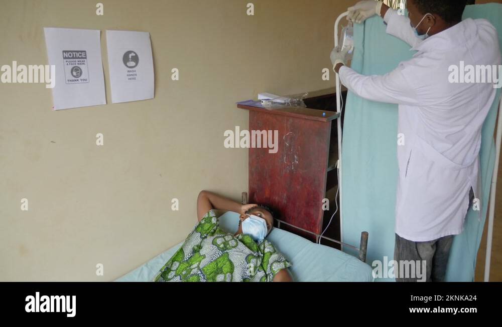 African male doctor injecting medicine into an IV drip on an African ...