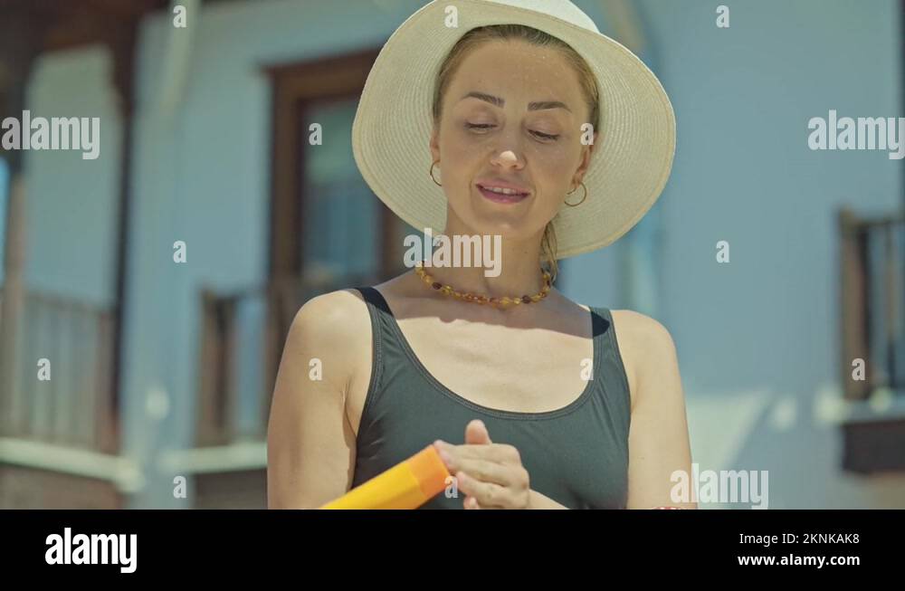 Beautiful lady applying sunscreen on her face by the swimming pool ...