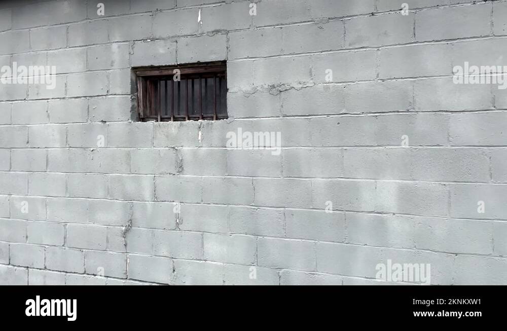 Pan of a spooky old concrete block jail with bars in windows Stock ...