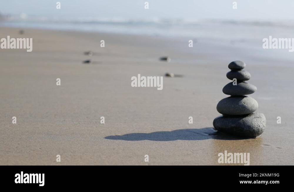 Rock balancing on ocean beach, stones stacking by sea water waves ...