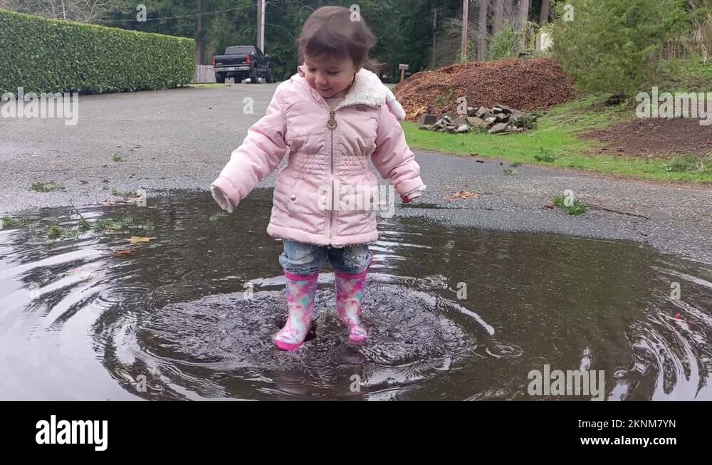 A cute little girl is so excited to be in a large puddle wearing pink ...