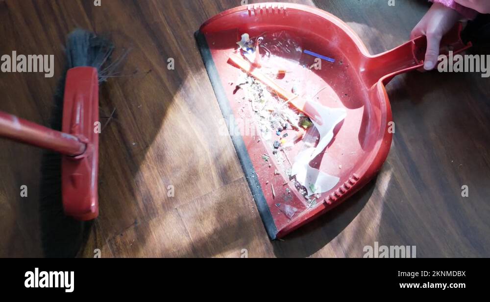 Sweeping dirty brown wood floor into dust pan with red broom and child ...