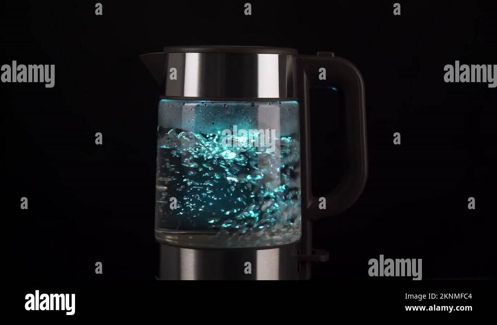 Boiling water in a glass electric kettle rises in bubbles in slow ...