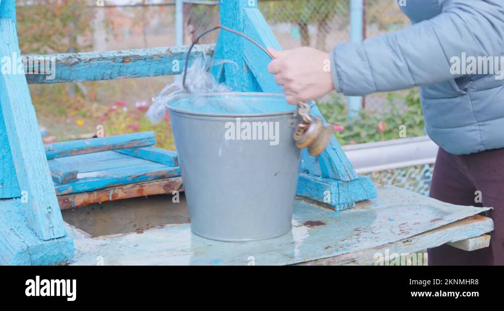 Person lifts bucket of drinking water from well by turning handle of ...