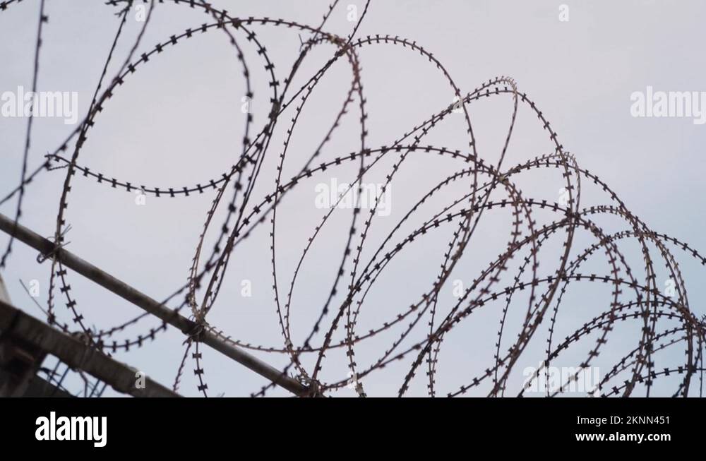 Metal fence with sharp barbed wire against blue sky. Restricted area ...