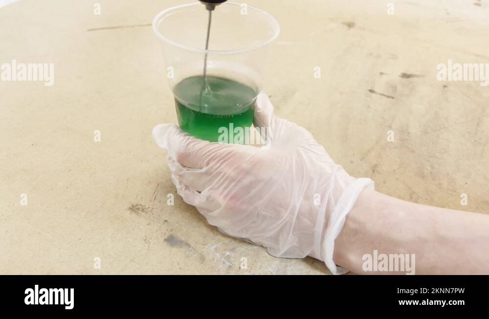 Gloved hands stir the green caustic liquid of green color in a plastic ...