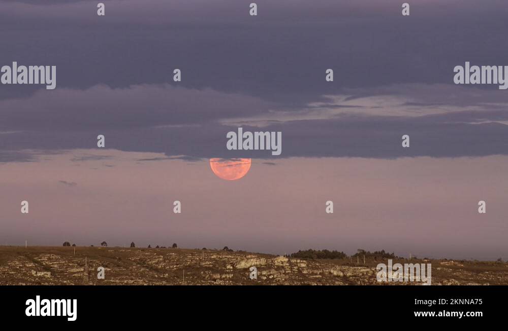 Rise of full glowing red moon with clouds above the horizon of the ...
