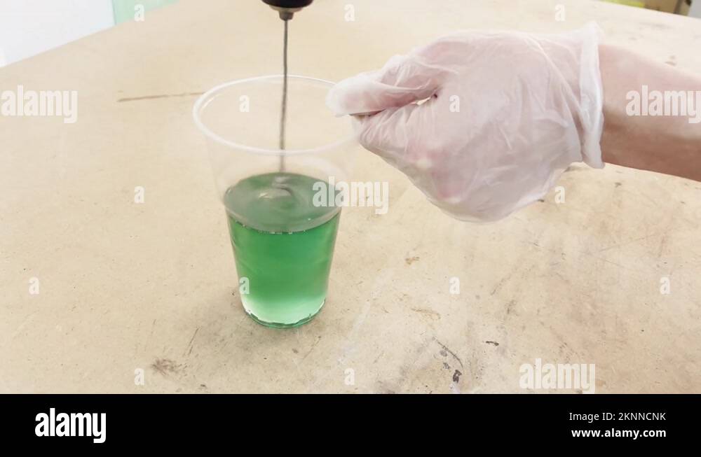 Gloved hands stir the green caustic liquid of green color in a plastic ...