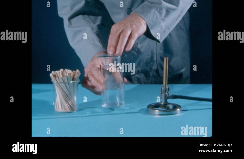 1960s: Beaker of wooden splints and bunsen burner in lab. Scientist ...