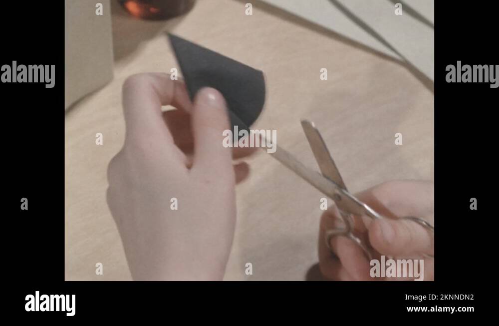 1960s: Hands cut a notch from a wedge shaped piece of folded paper ...