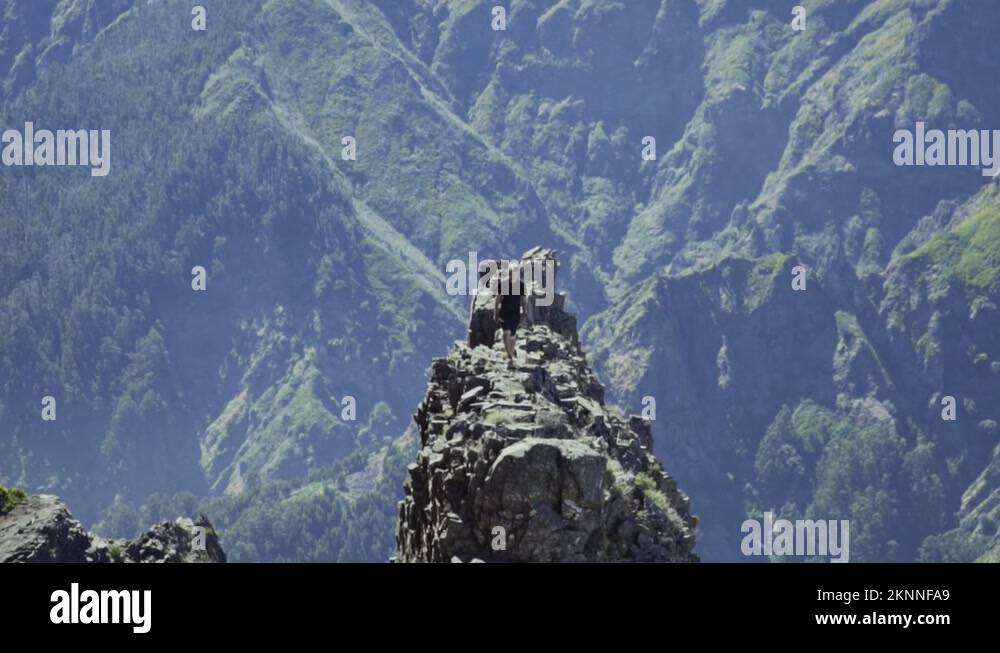 Climber walks down rock formation in mountains with steep drop on each ...