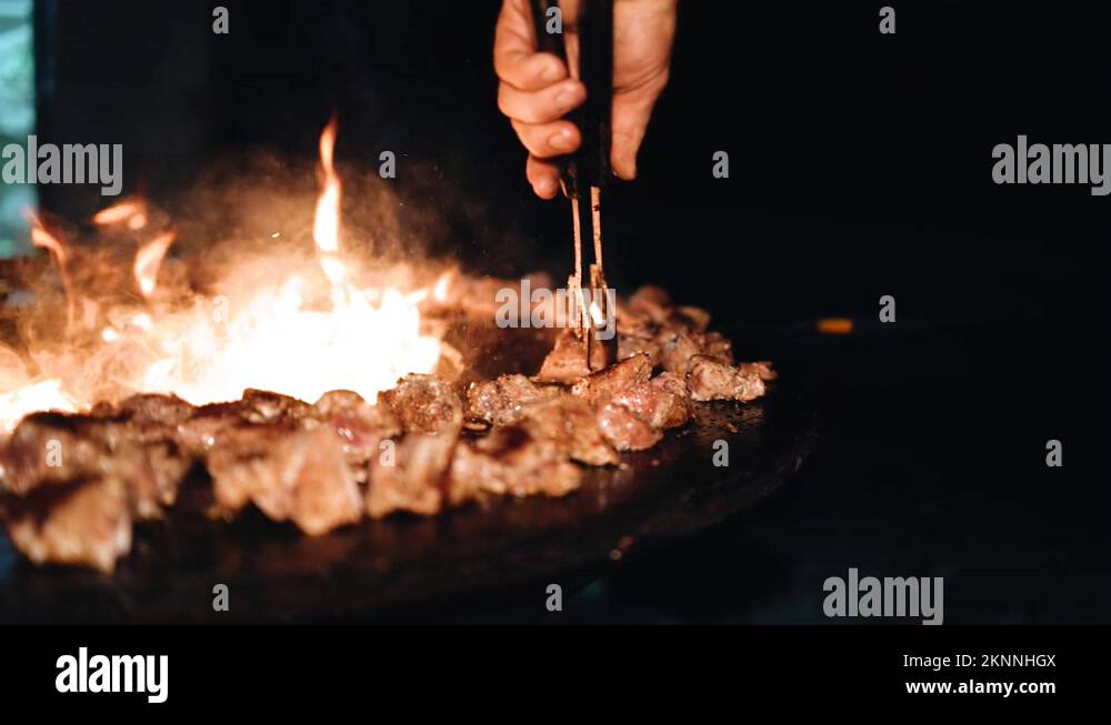The cook cooks meat on the grill at night. Cooking fried meat. Close-up ...