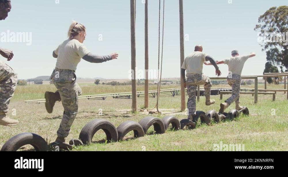 Diverse group ale soldiers running on car tyres at army obstacle course ...