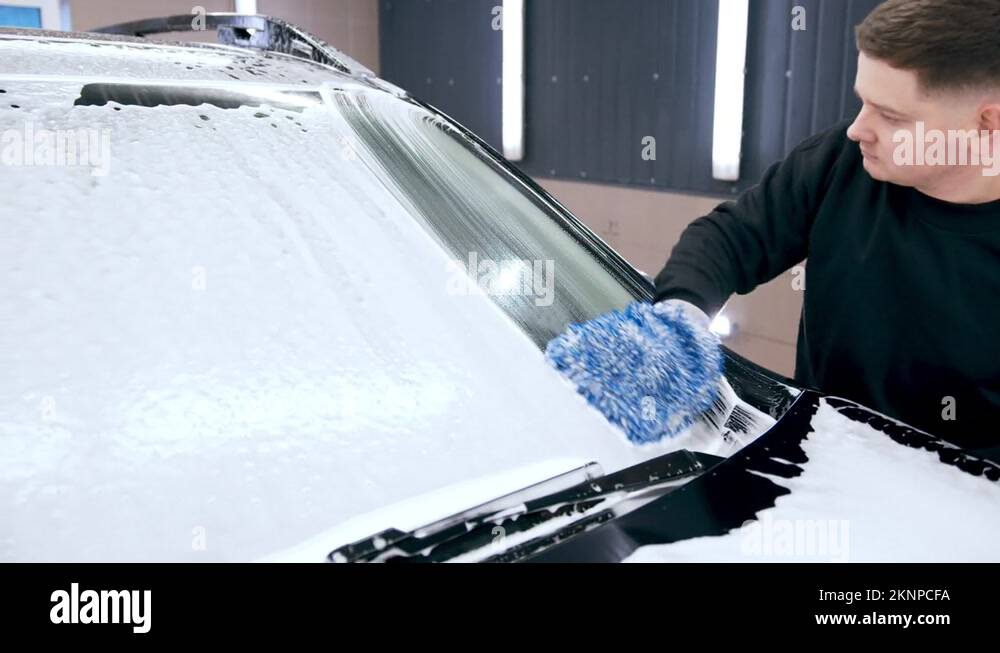 Professional worker is washing windshield of car by special cleaning ...