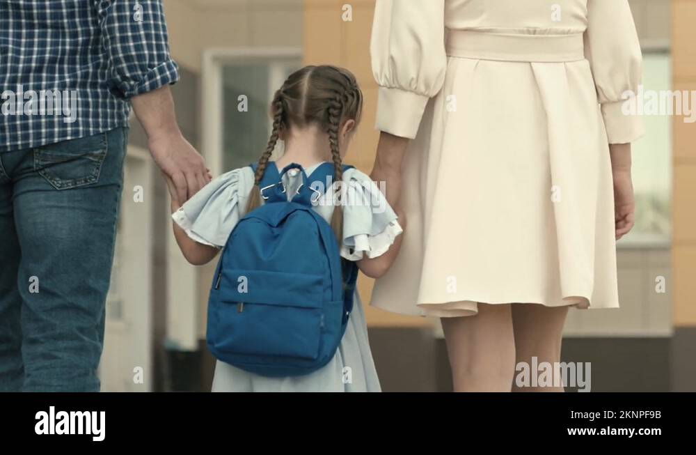 little girl goes hand in hand with parents to school, kid with a ...