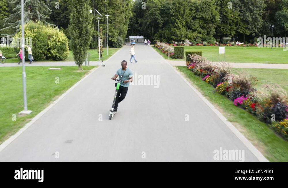 Male young black man rides e-scooter on park pathway, drone dolly out ...